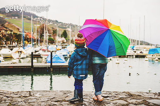 Two cute kids resting by the lake on a rainy day, hiding under big ...