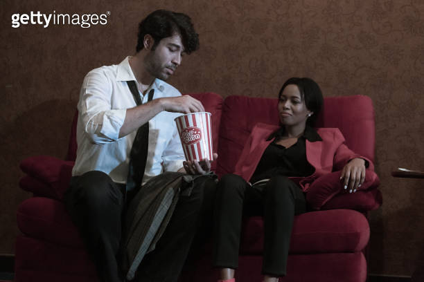 Couple eating popcorn while waiting to get in to cinema for watching ...