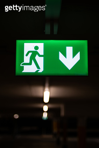 Illuminated green exit sign suspended in a dark car parking lot shallow ...