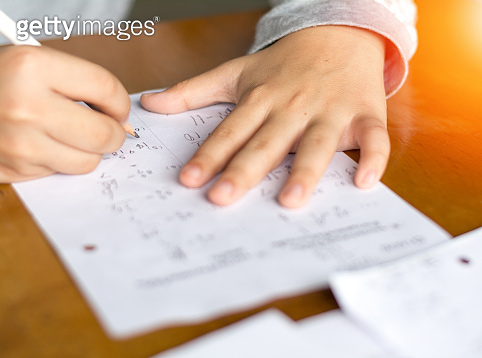 Close up kid's hand writing on paper, writing messy math on wooden ...