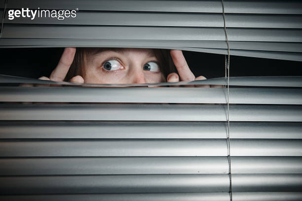 Startled and scared, a young woman peeps sideways through blinds 이미지 ...