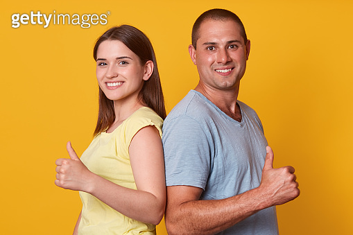 Manetic cheerful man standing back to back to young brunette woman ...