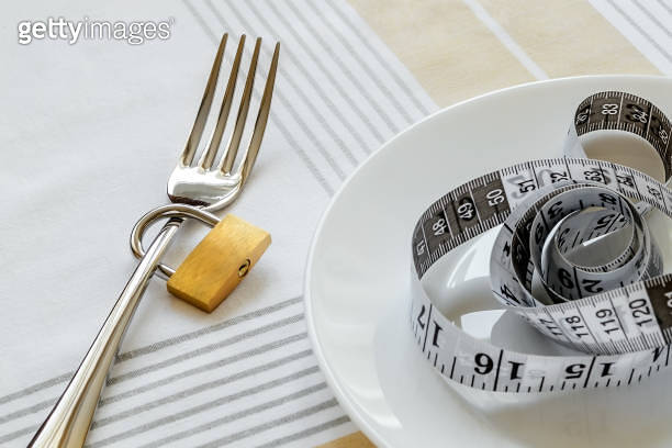 Metal fork locked with padlock and white plate with measuring tape on a ...