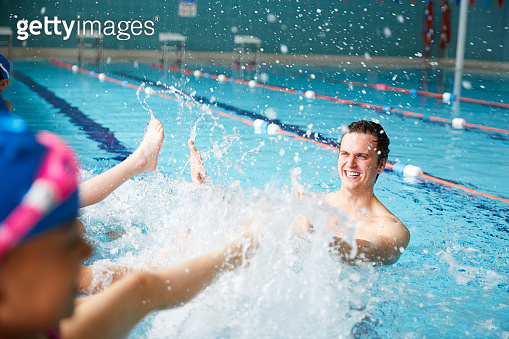 Coach In Water Gives Children Swimming Lesson As They Sit On Edge Of ...
