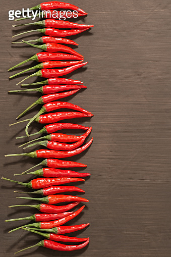 Row of small red hot chili peppers vertically arranged on brown ...