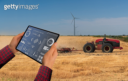 A farmer with digital tablet controls an autonomous tractor (1157777890 ...