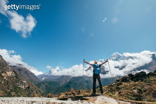 Young hiker backpacker man rising arms with trekking poles enjoying the ...