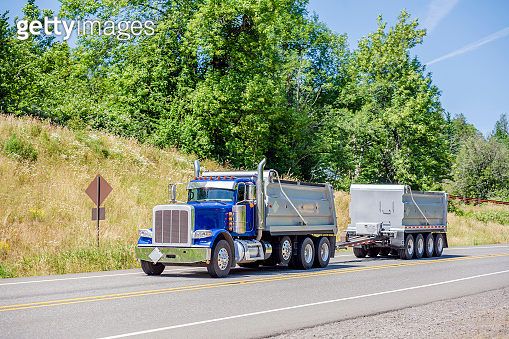 Blue big rig semi truck tipper with two tip trailers going on the road ...