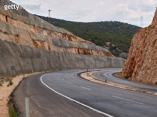 Asphalt road curves between two rock cliffs with openwork power line ...