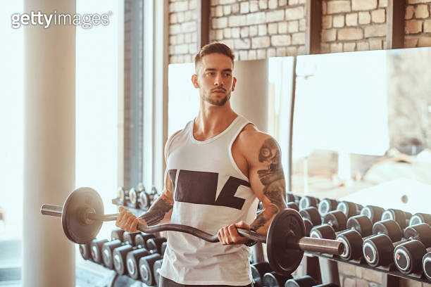 Attractive tattooed bodybuilder is doing his exercises with barbell in ...