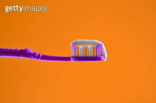 Toothpaste on a violet toothbrush close-up on an orange light ...