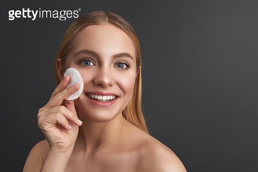 Excited young woman smiling while pressing cotton pad to her face 이미지 ...