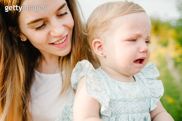 Portrait of a little beautiful baby girl crying and mom on nature on ...