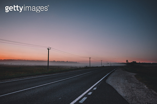 Morning has come. The orange sun rises above a misty field, asphalt ...