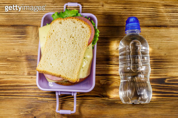 Lunch box with sandwiches and bottle of water on a wooden table. Top ...