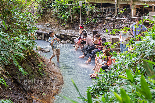 People relaxing and dipping their toes into the gray onsen river at ...