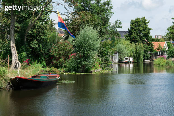 Rowing boat, green trees and houses along water in Broek op Langedijk ...