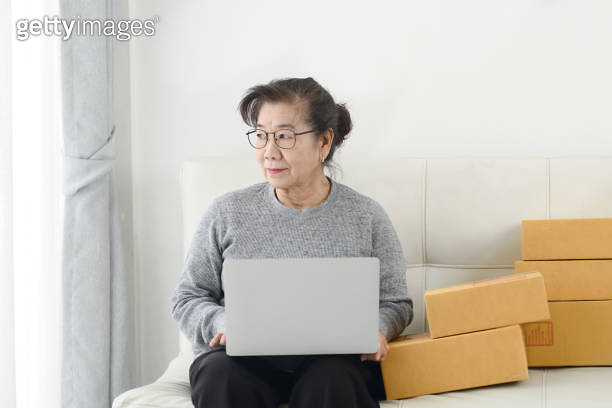 Asian senior woman using laptop while selling online with packaging ...