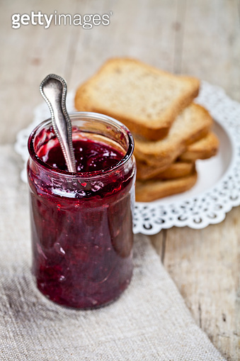 Homemade cherry jam in glassjar and fresh toasted cereal bread slices ...