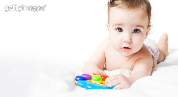 Cute baby girl in diaper playing with rattle on white bed in your room ...