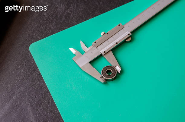 Ball bearing and vernier caliper on a black and turquoise background ...