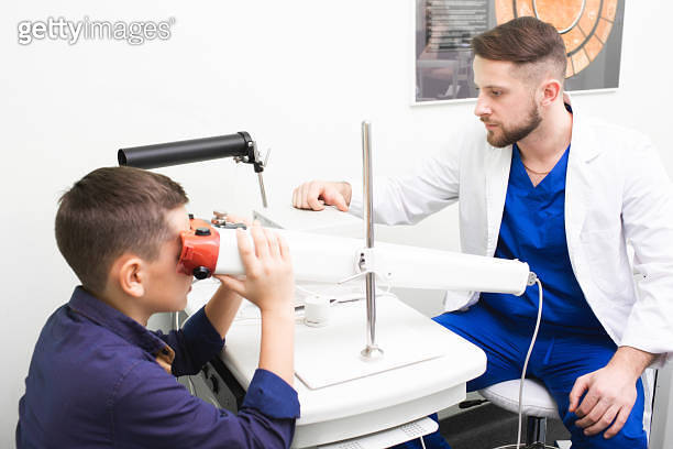 Boy looking into device to stimulate vision. Man ophthalmologist ...