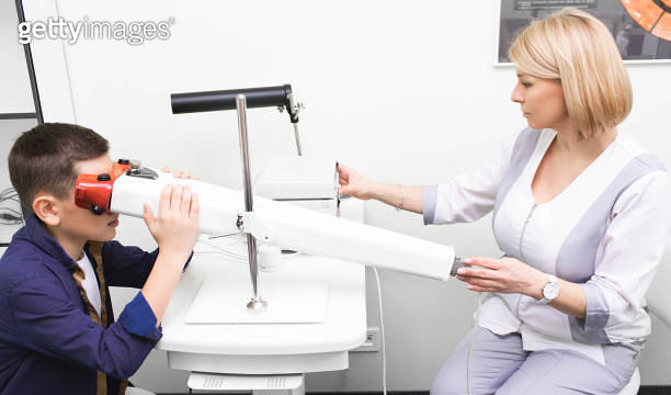 Boy looking into device to stimulate vision. Female ophthalmologist ...