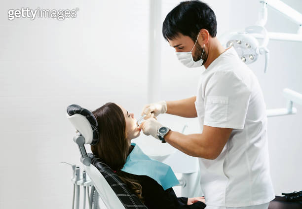Young woman at dentist clinic office. Male doctor performing extraction ...
