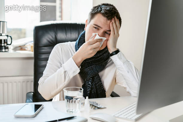 A young freelancer, businessman or office worker sneezes, coughs, blows ...