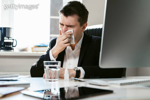 A young businessman or office worker sneezes, coughs, blows his nose at ...