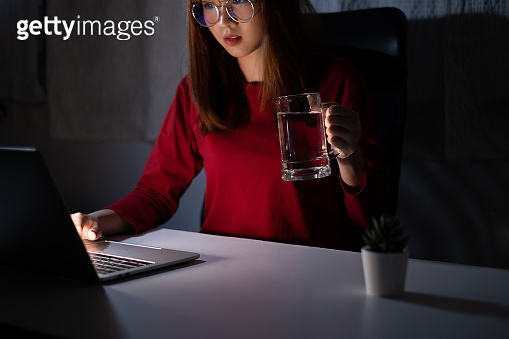 Asian woman working late time with laptop computer drinking water home ...
