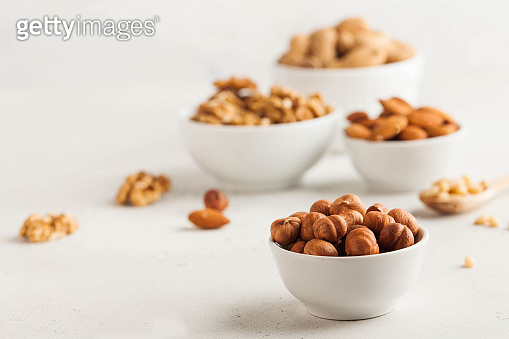 A handful of hazelnuts in a white bowl, assorted nuts on a light ...