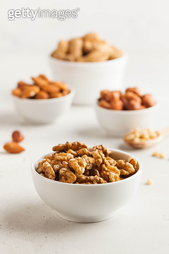 A handful of walnuts in a white bowl, assorted nuts on a light ...