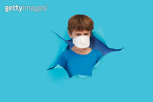 Child boy wearing medical face mask poses through torn paper hole ...