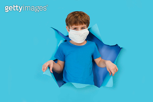 Child boy wearing medical face mask poses through torn paper hole ...
