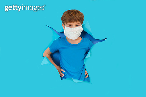 Child boy wearing medical face mask poses through torn paper hole ...