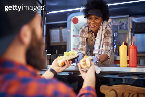 polite afro-american female employee holding, giving, two sandwiches to ...