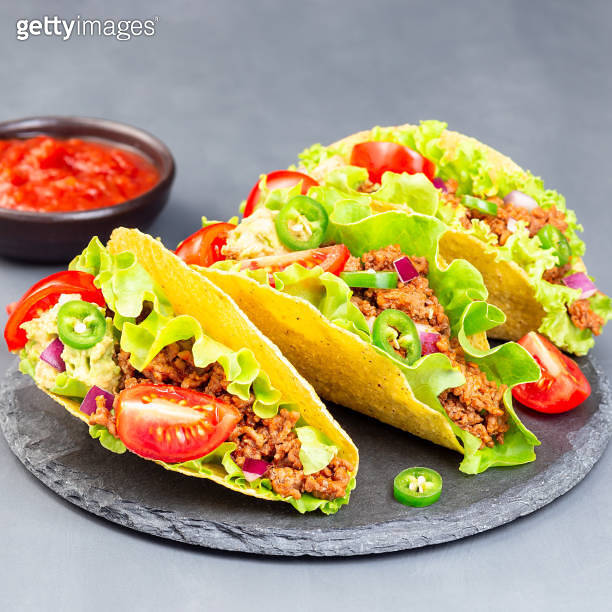 Taco shells with lettuce, ground beef meat, mashed avocado, tomato, red ...