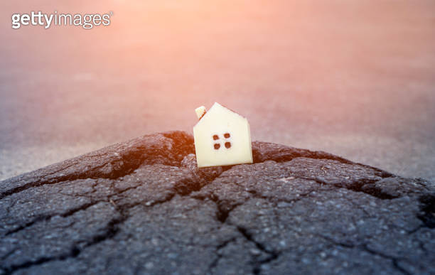 Miniature toy house standing on the damaged asphalt road. Earthquake ...