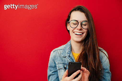 Portrait of happy young woman in eyeglasses laughing using smartphones ...