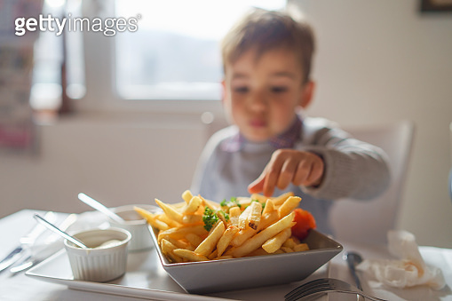 Portrait of small little cute caucasian boy kid eating french fries ...