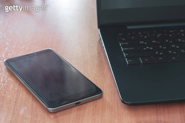 Black laptop and cell phone on the table. Selective shallow focus on ...