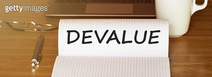Word DEVALUATION composed of wooden letter. Stacks of coins in the ...