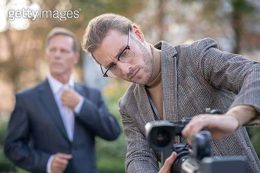 Fair-haired male journalist fitting camera to tripod, getting ready for ...
