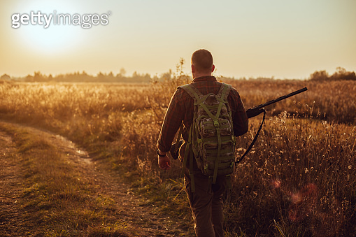 Strong young hunter with red beard holding his gun and walking along ...