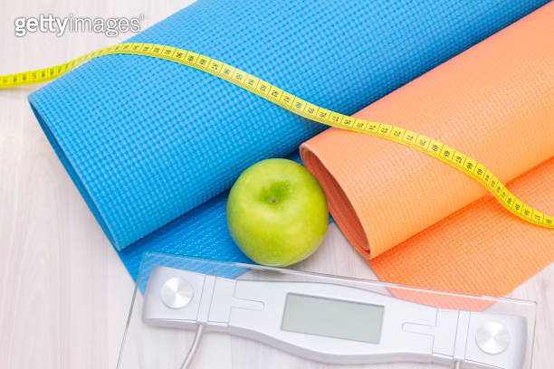 scales, green apple, measuring tape and sports mats on a light wooden ...