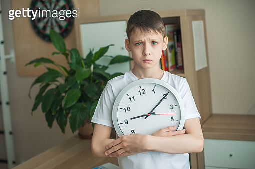 A teenager boy in a children's room stands with a big clock in his ...