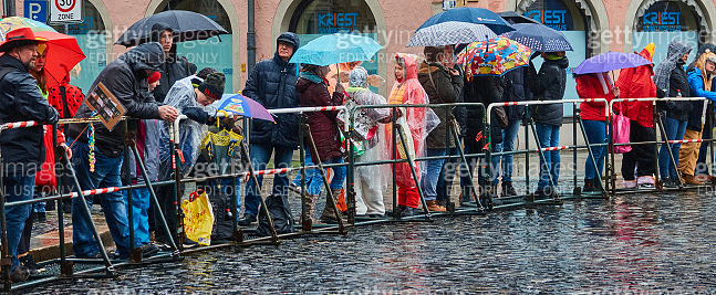 Spectators with rain protection, rain jackets and umbrellas wait behind ...