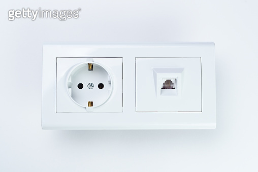 An electrical outlet and a white telephone socket are located side by ...