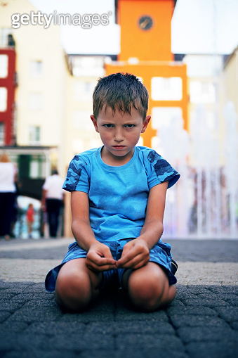 Angry offended child sits on the ground in the street and looks with an ...